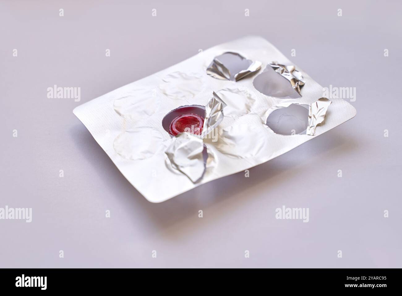 Open blister pack with one remaining red pill on light background ...