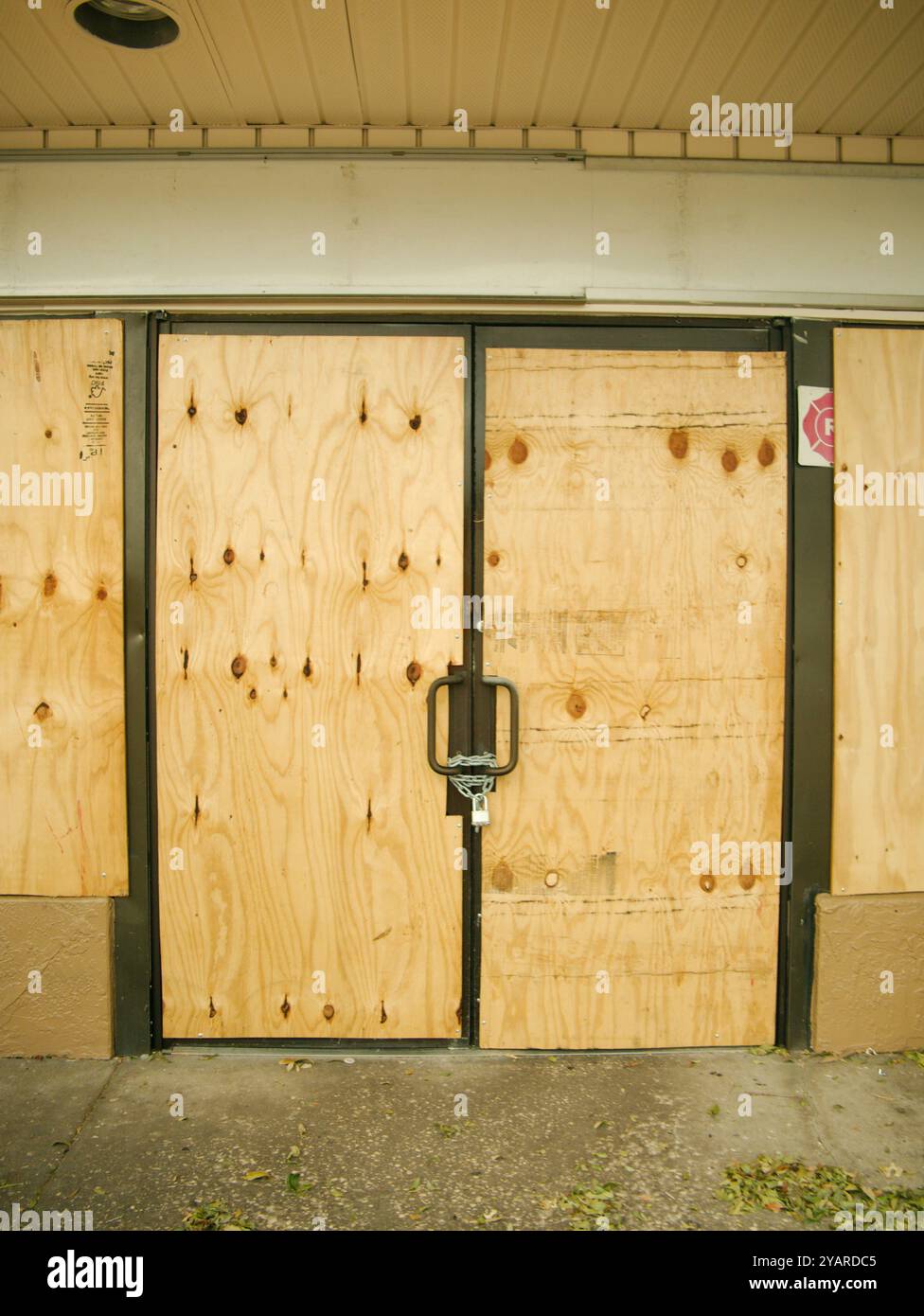 Locked Plywood covered double doors of a store front and side windows ...