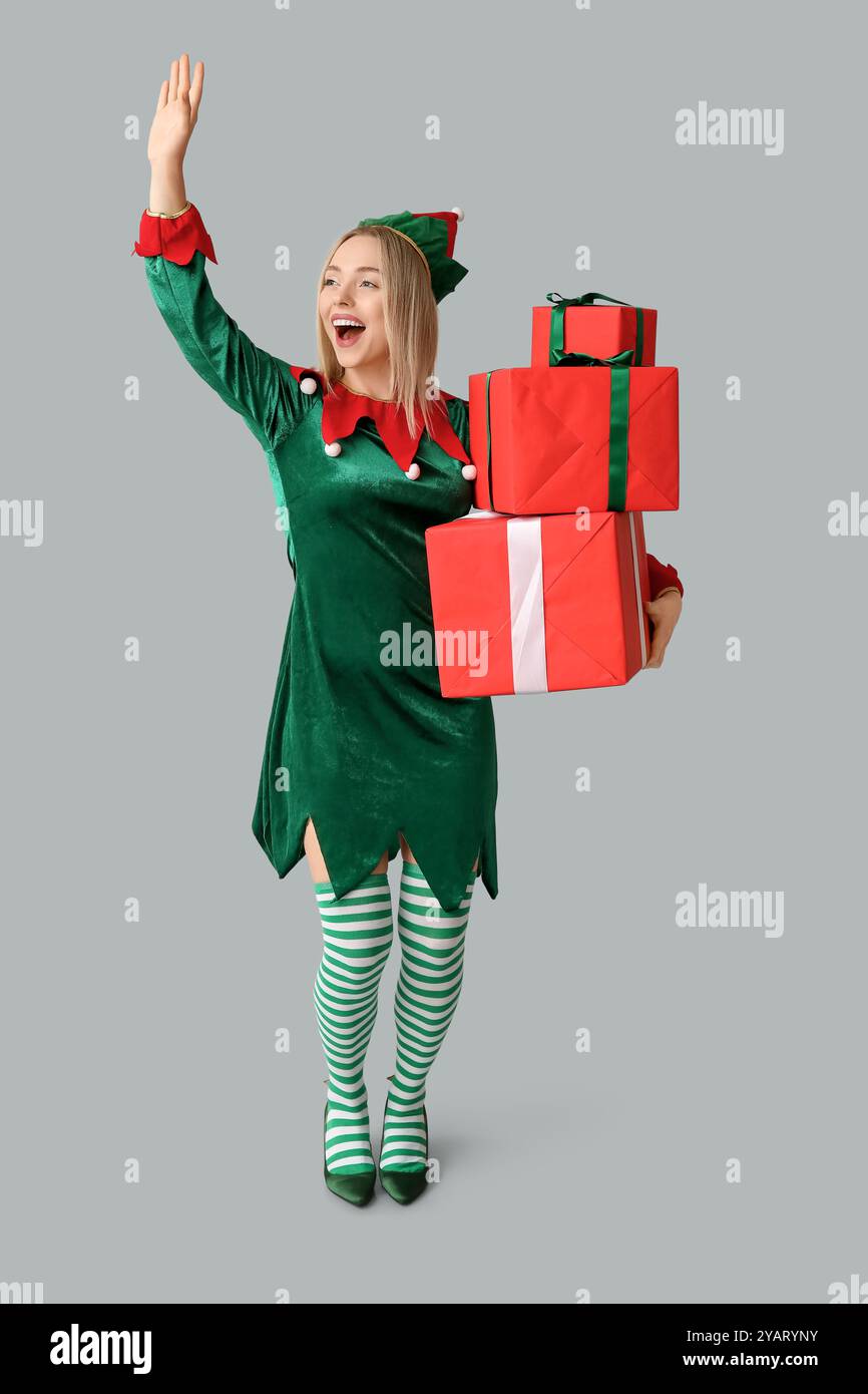 Young woman in elf costume holding Christmas gift boxes and waving hand ...