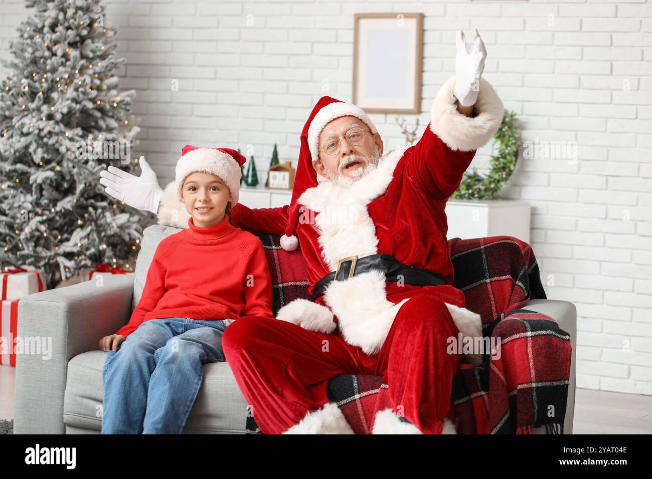 Santa Claus and cute little girl sitting on sofa in decorated room for ...