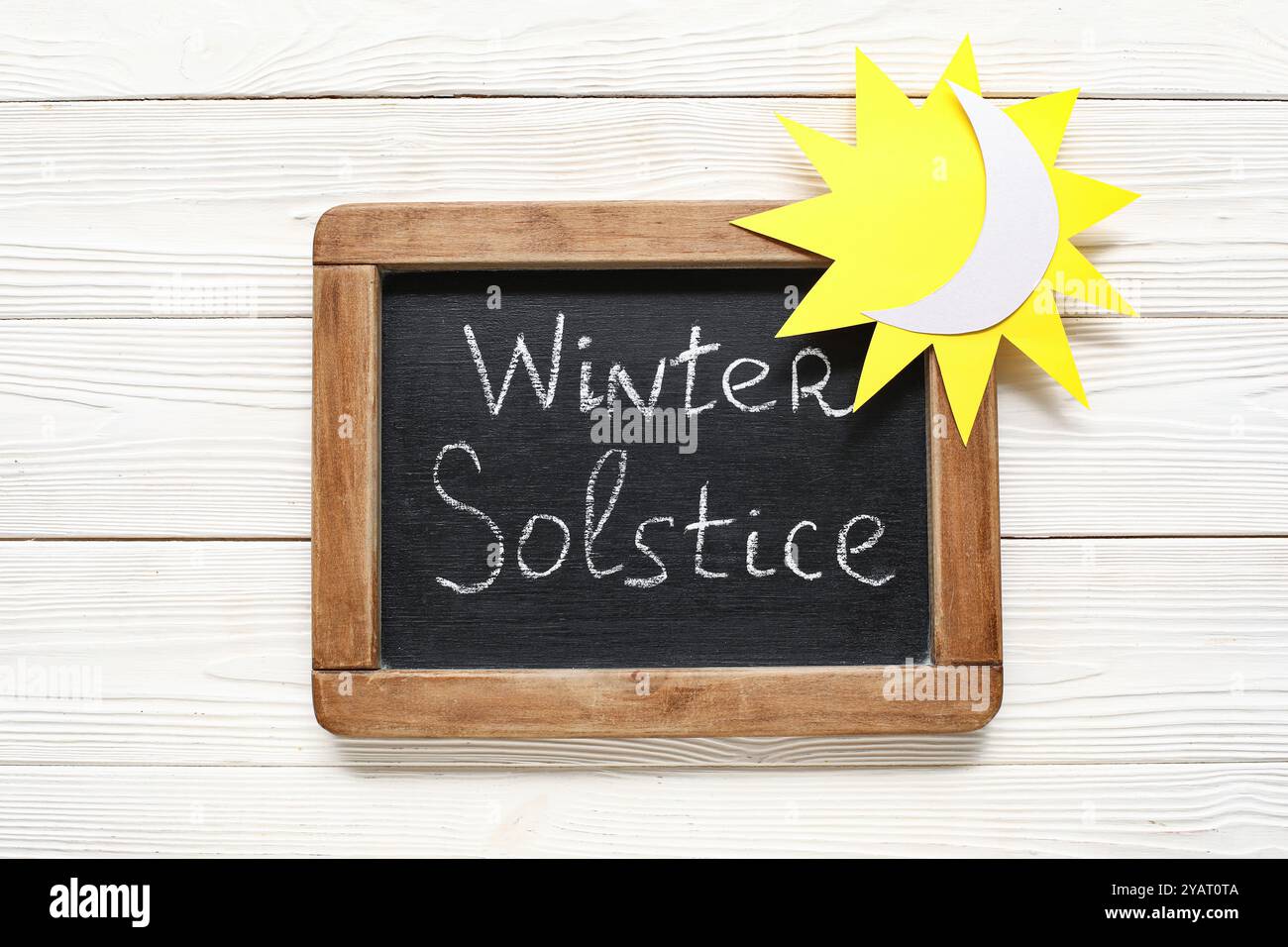 Chalkboard with text WINTER SOLSTICE and paper sun on white wooden ...