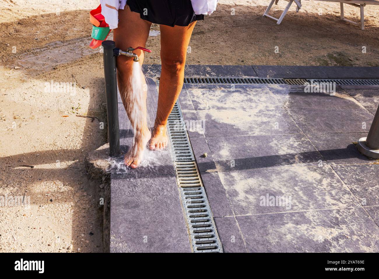 Woman rinsing sandy feet under beachside shower after day on sand ...