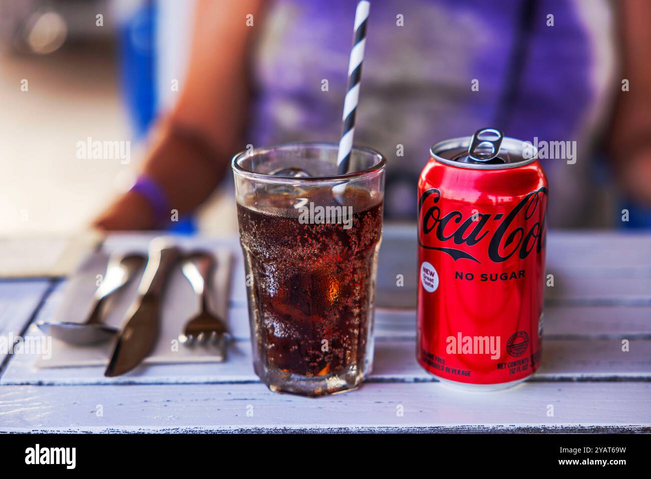 Glass of cola with ice and striped straw alongside can of Coca-Cola No ...