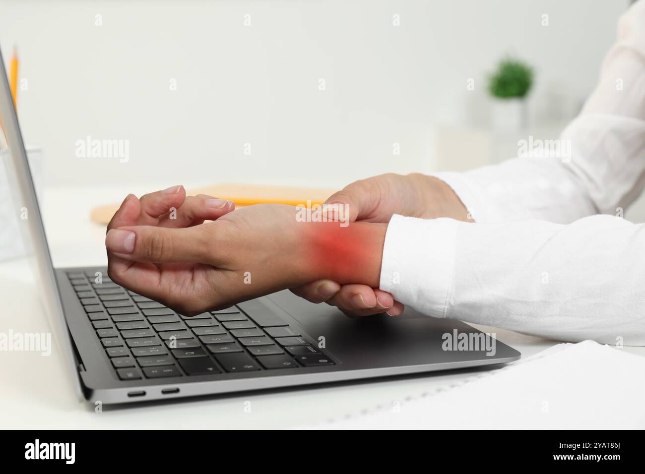 Woman suffering from pain in wrist at white table with laptop, closeup ...