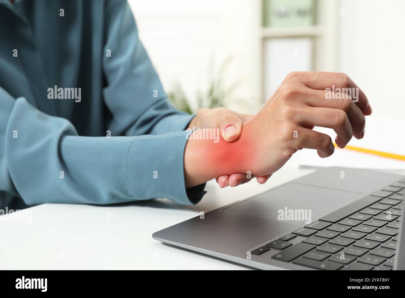 Woman suffering from pain in wrist at white table with laptop, closeup ...