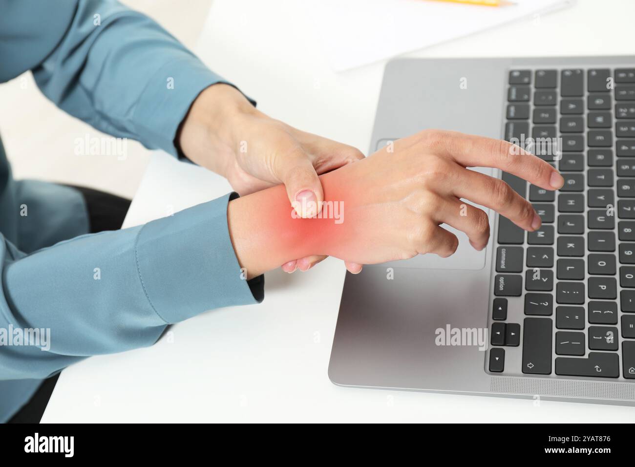 Woman suffering from pain in wrist at white table with laptop, closeup ...