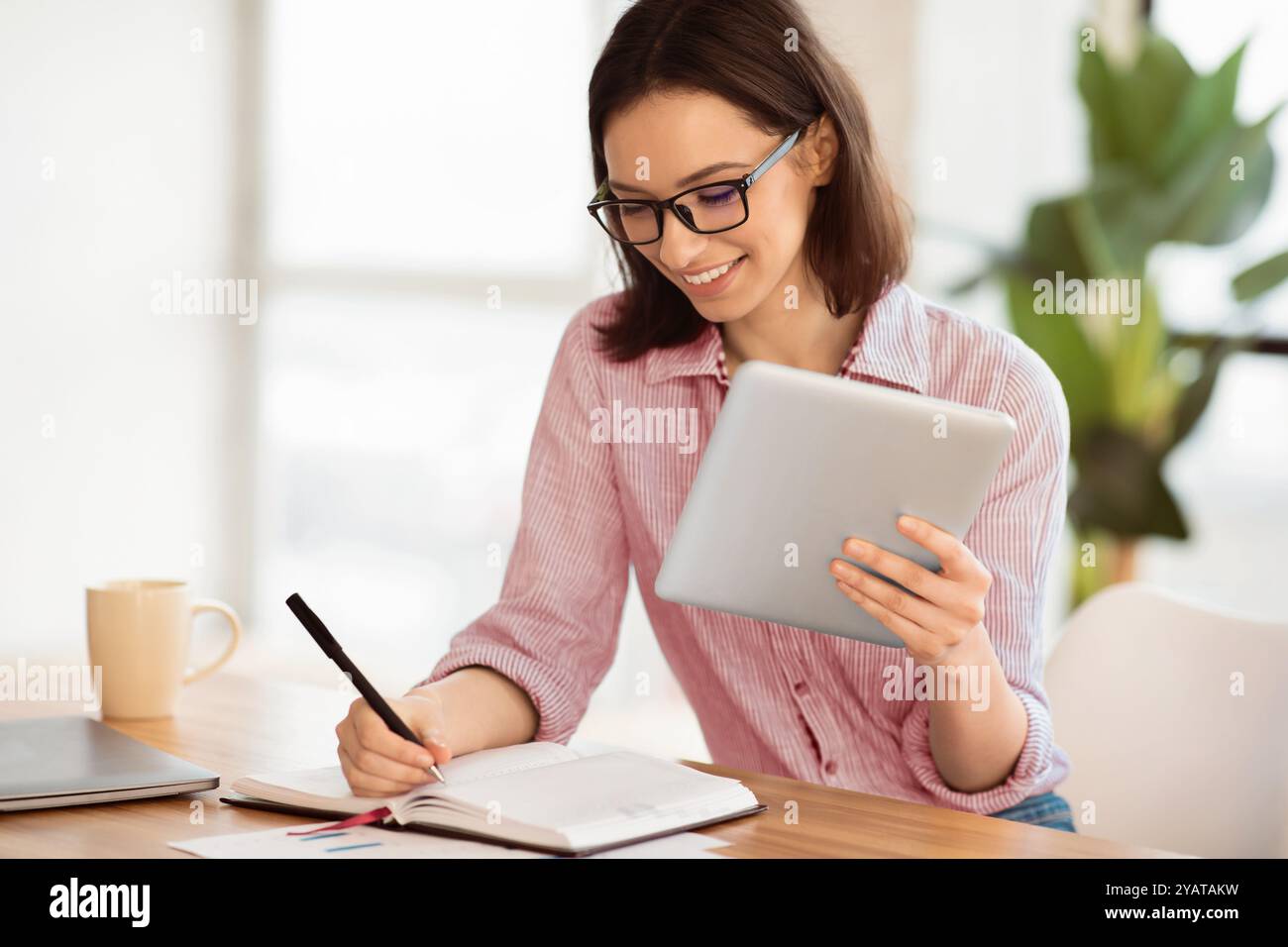 Left-handed girl holding tablet and writing in notebook Stock Photo - Alamy