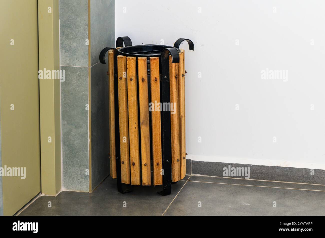 The wooden trash bin stands propped in a corner, its striped design ...