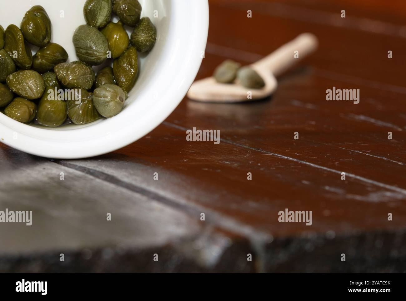 Capers inside a white ceramic pot that is lying down, and a wooden ...