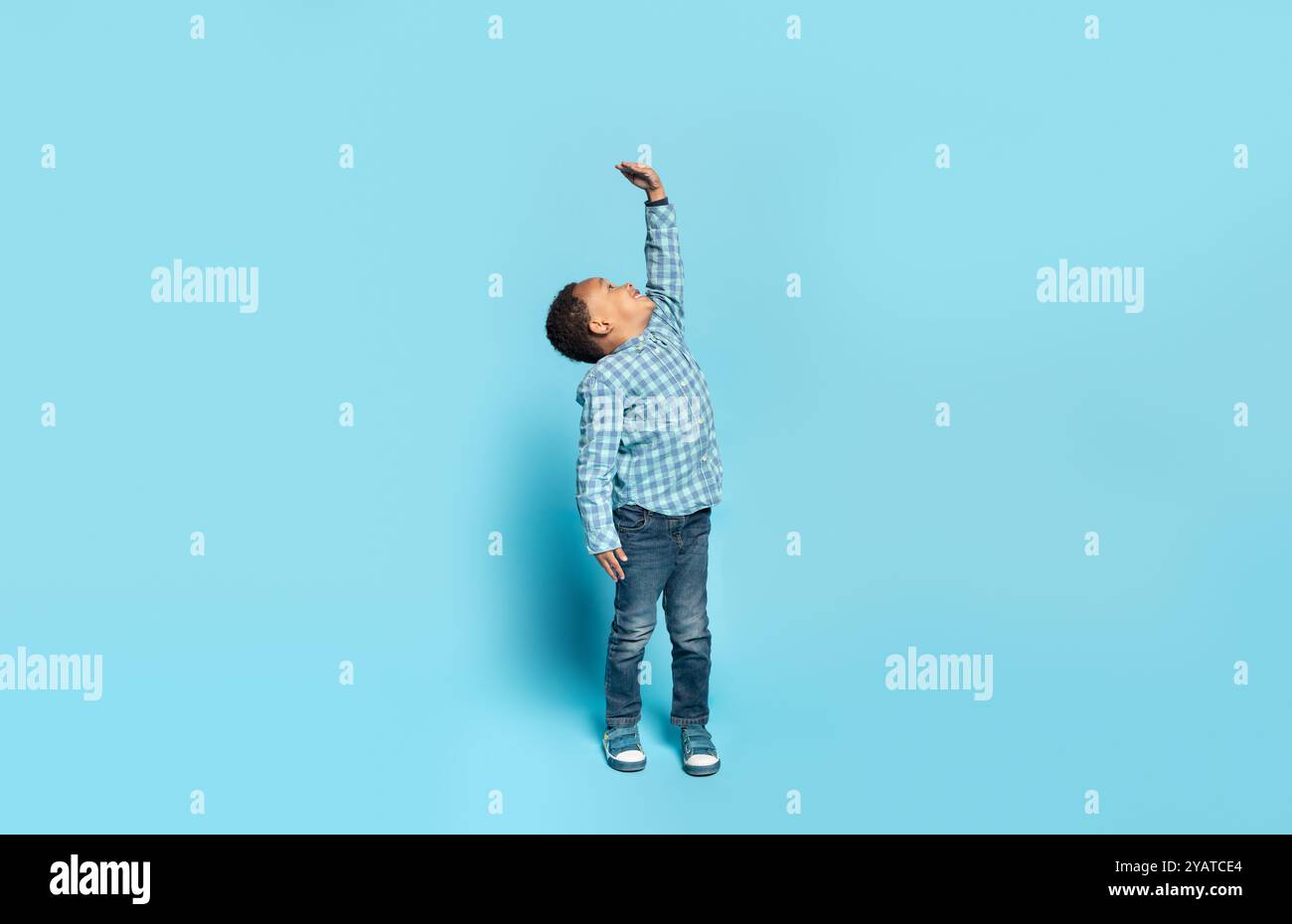 Little african american boy wishes he were taller, raising his hand to ...