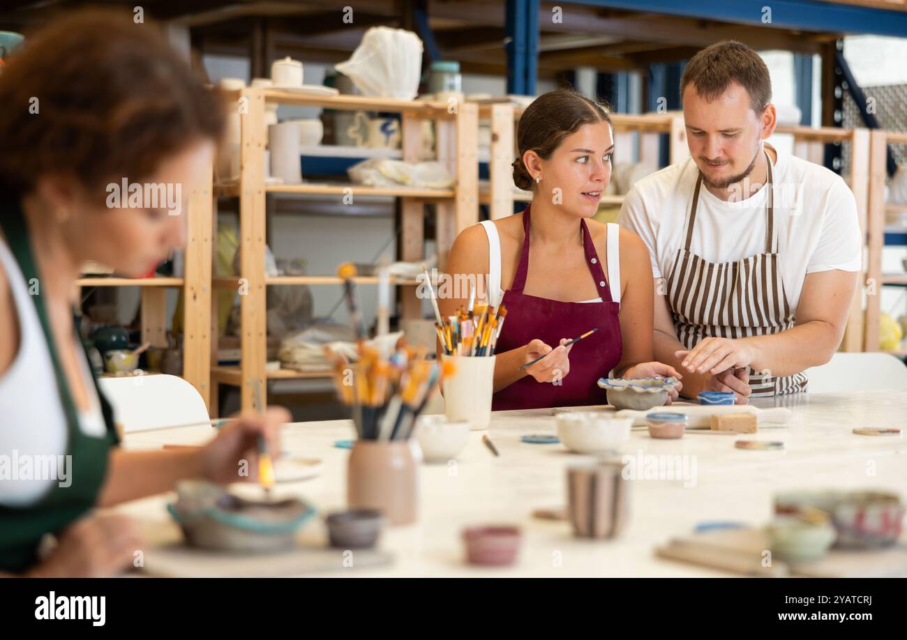 During master class, student paints clay vessel under guidance of male ...