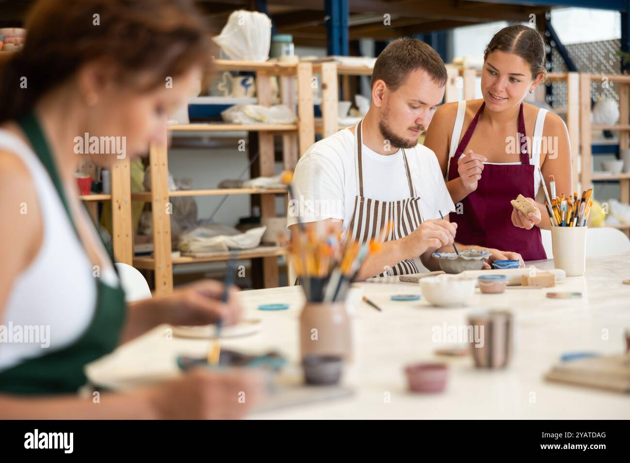 During master class, student paints clay vessel under guidance of ...