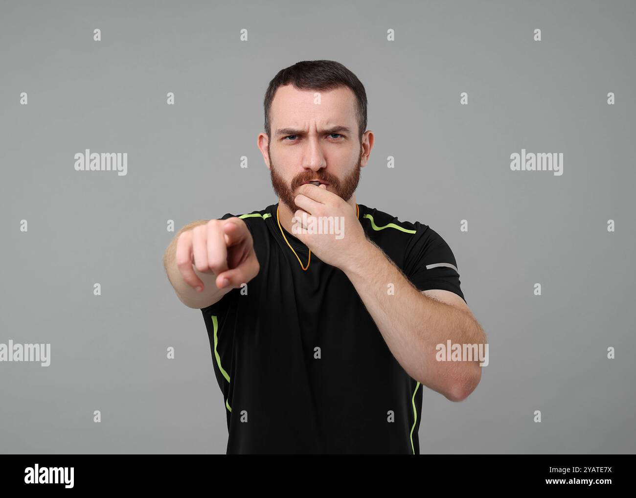 Young man blowing whistle on grey background Stock Photo - Alamy