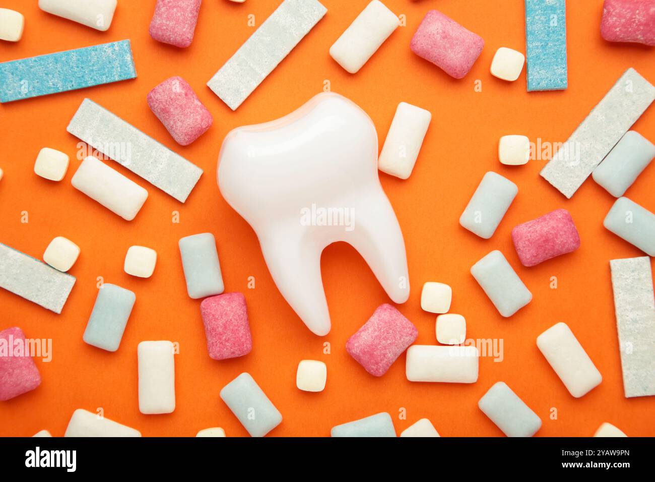 White healthy tooth model and heap of chewing gums on orange background ...