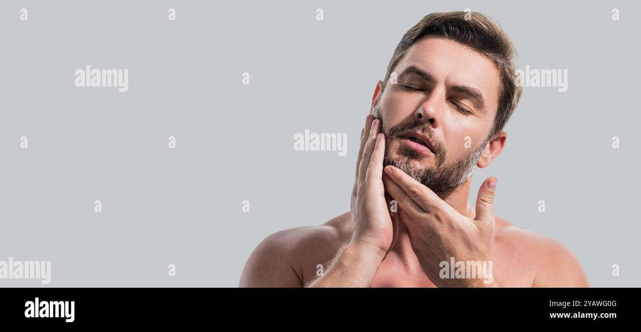 Close up beauty portrait of satisfied man after facial cream. Attractive brunet guy touching ...