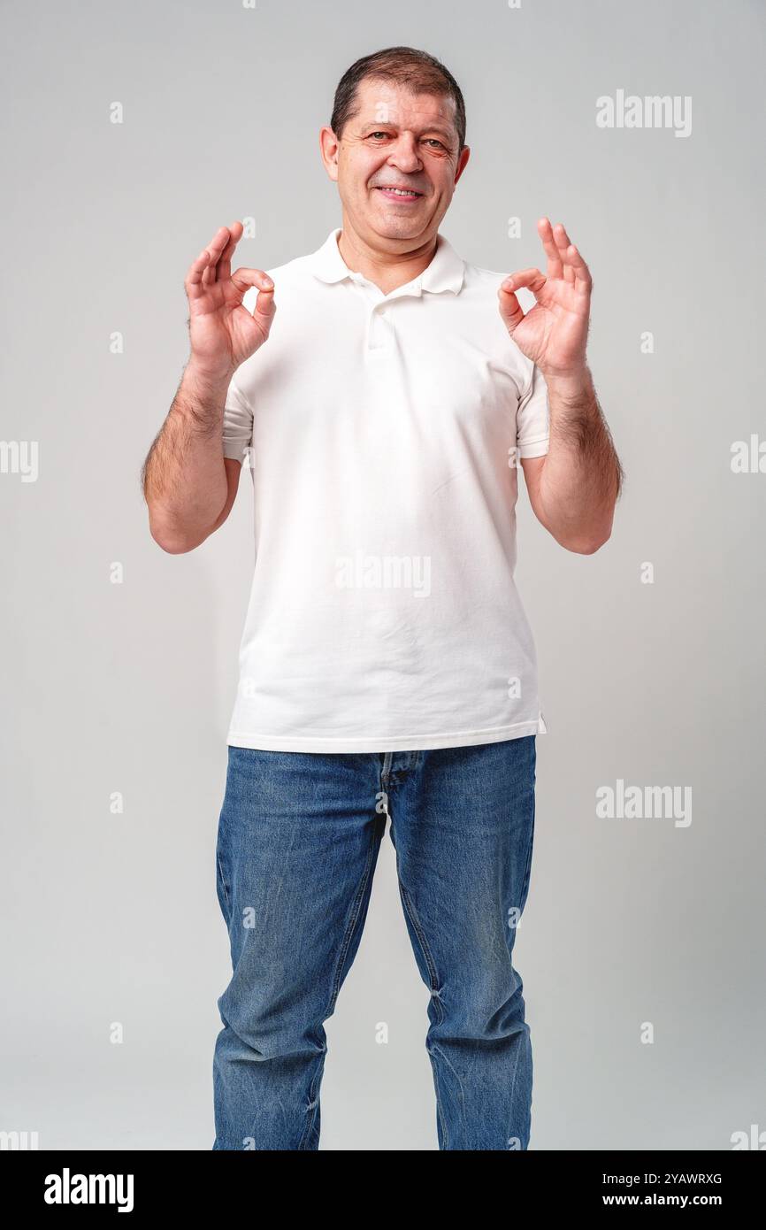 A man in a white shirt poses with a cheerful expression showing OK hand ...