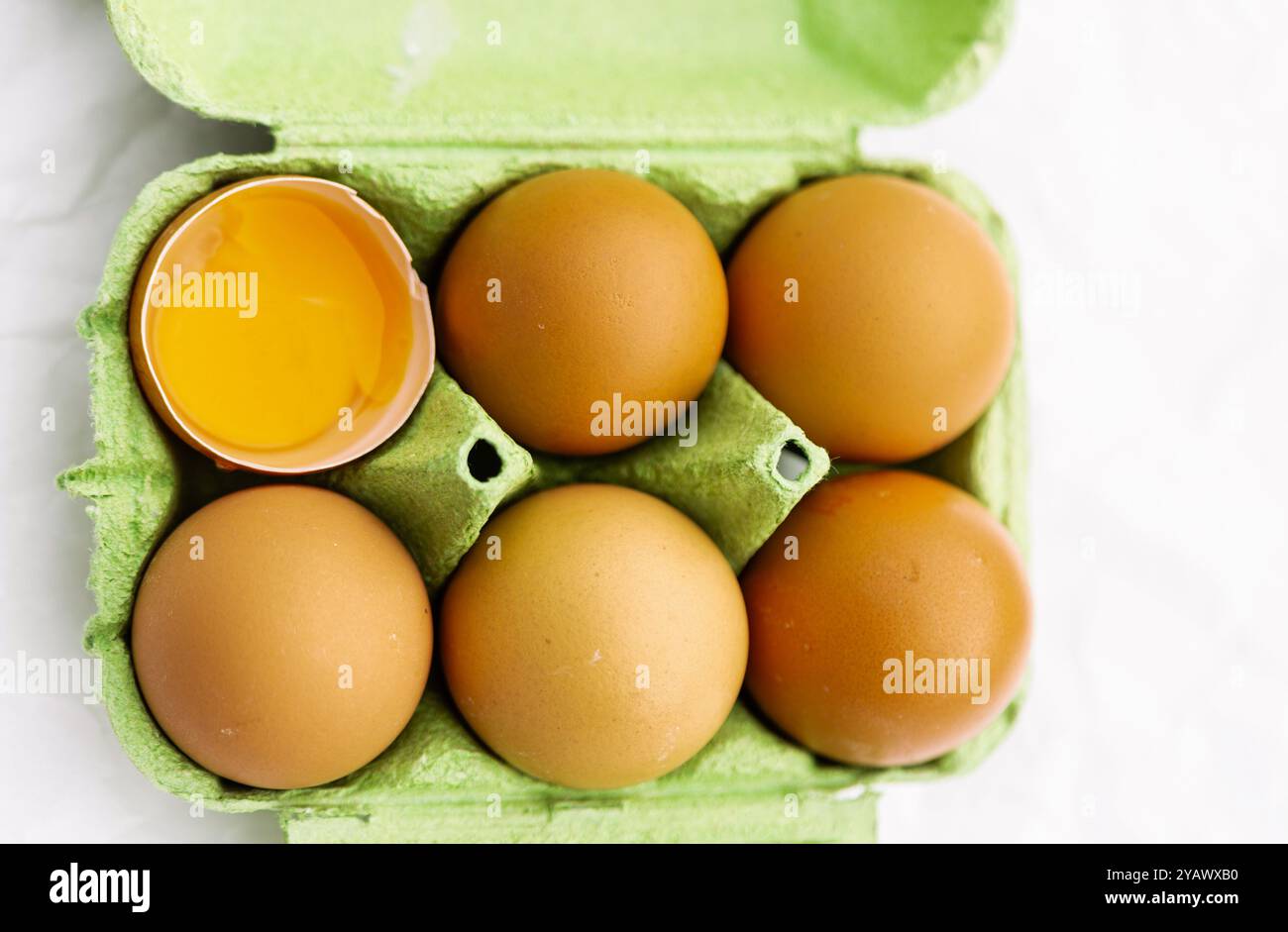 Close-up of a green egg carton holding five brown eggs and one egg with ...
