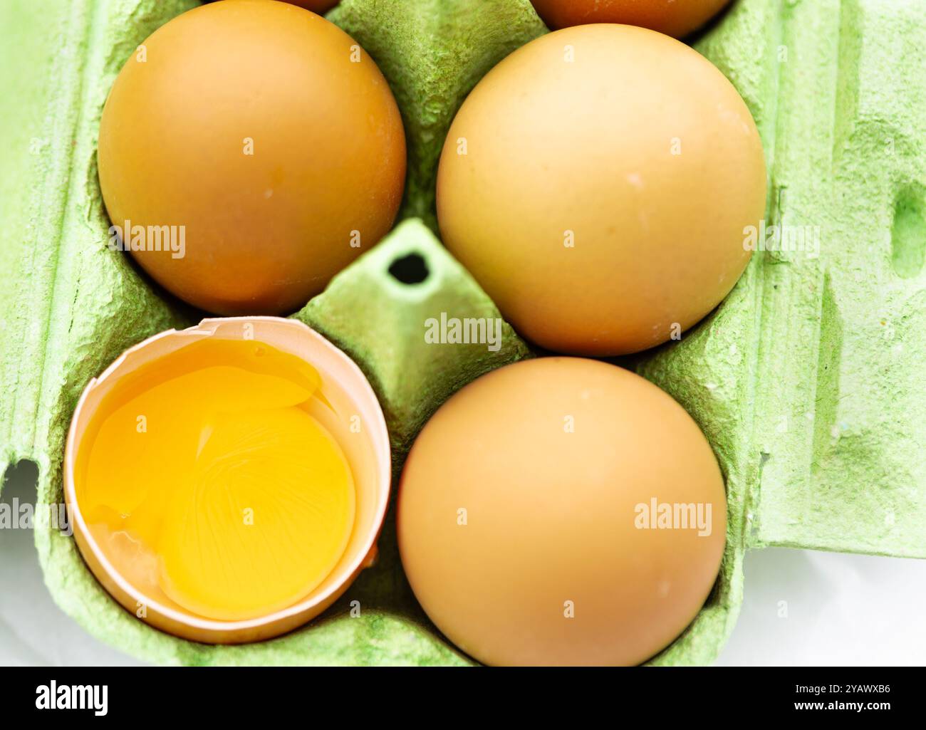 Close-up of a green egg carton containing three brown eggs and one egg ...