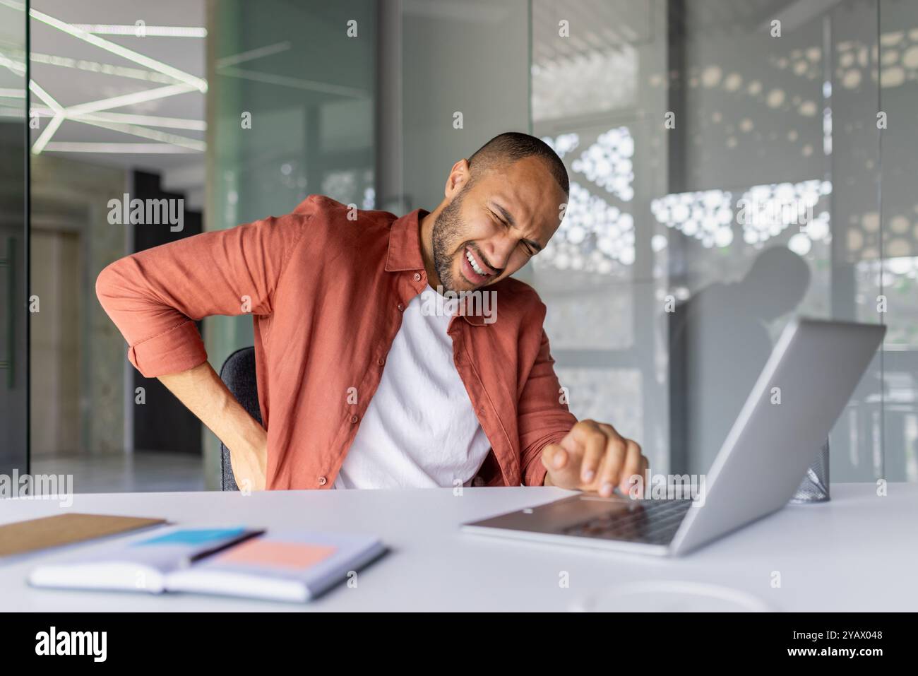 Man experiencing back pain while working at office desk with laptop ...