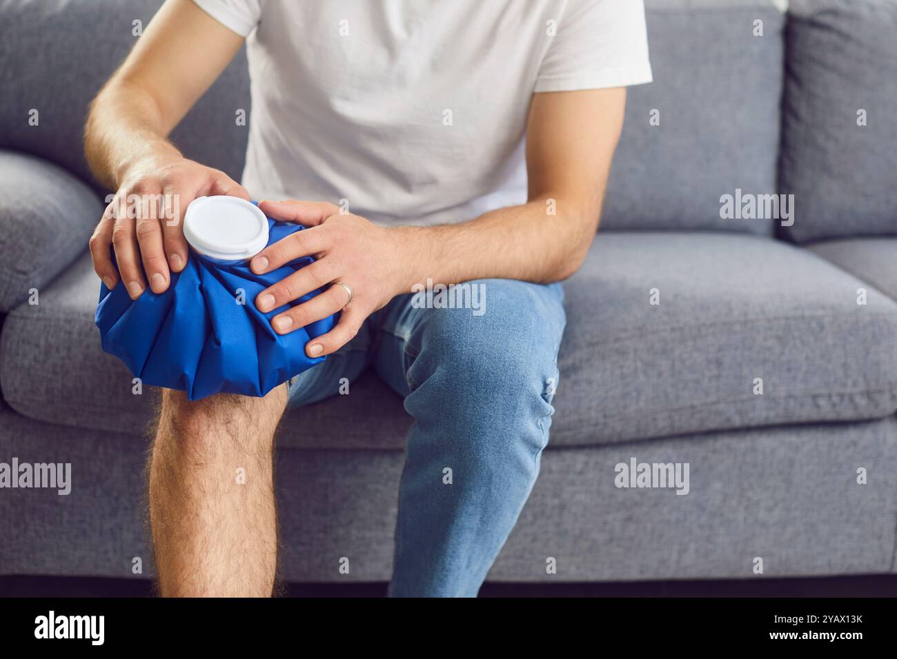 Man with a cold compress pouch on his injured knee is sitting on the ...