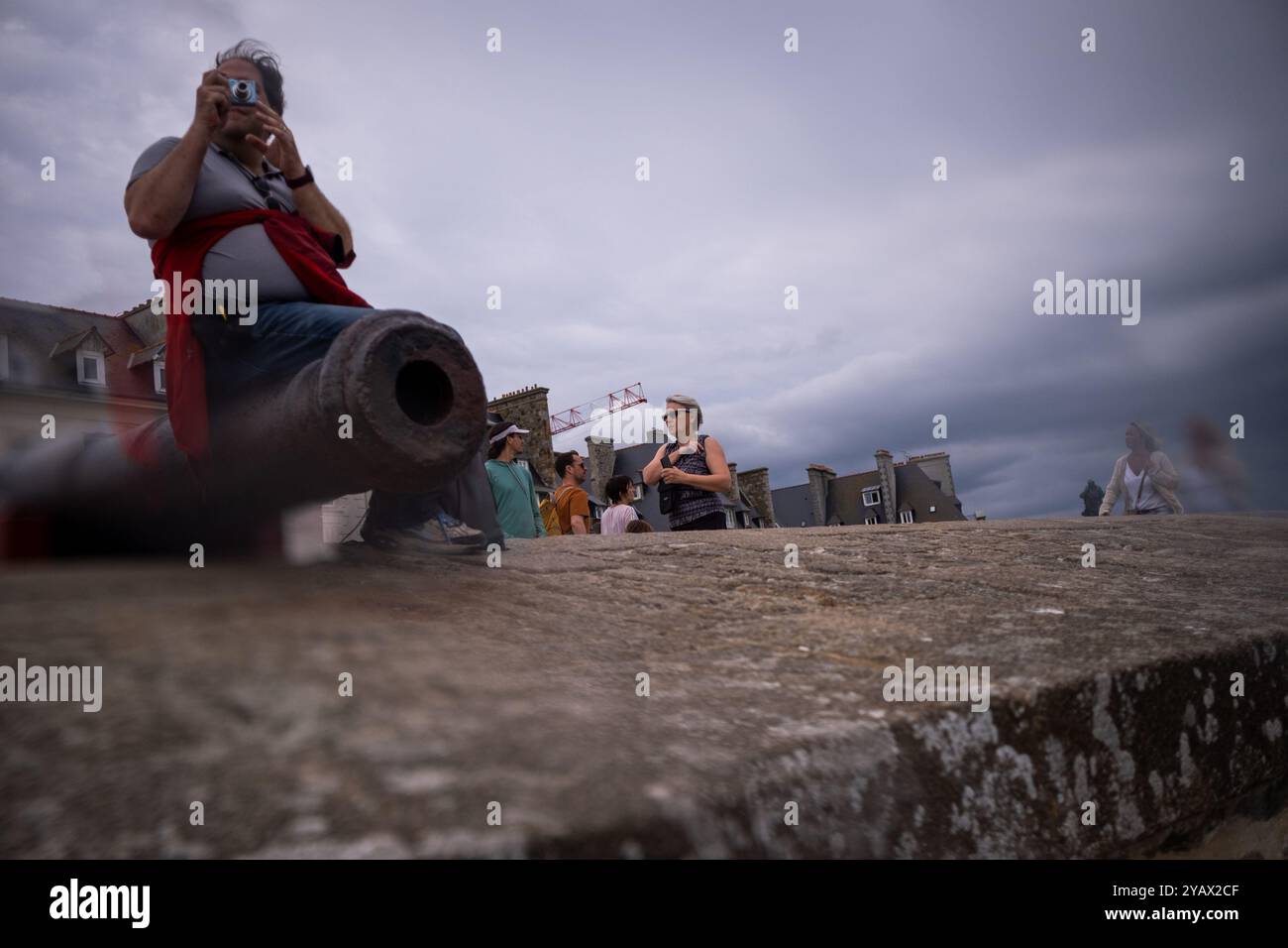 Tourist sitting on a cannon taking photos of the sea with a compact ...