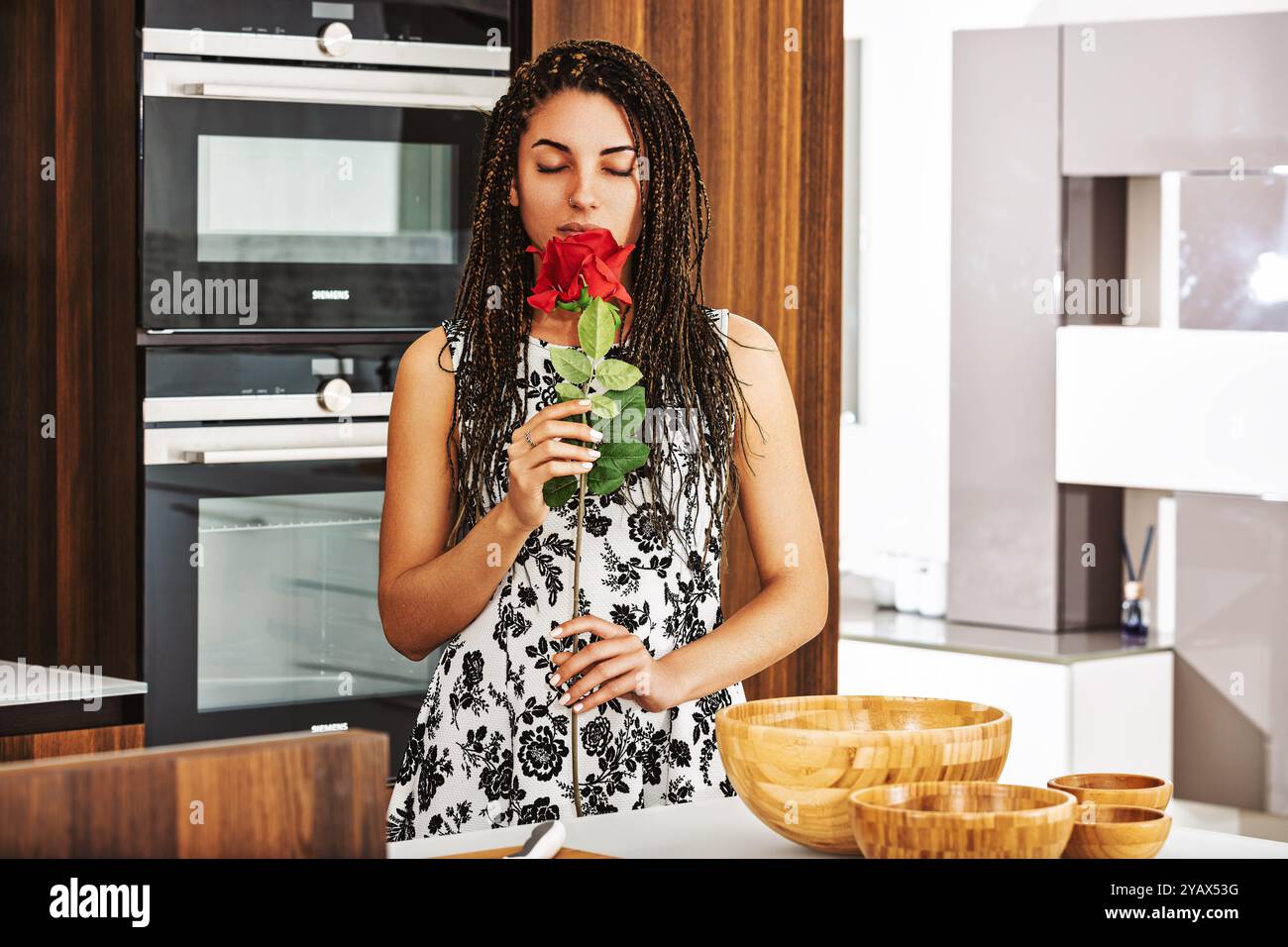Young woman with long braids stands in her modern kitchen, holding a ...