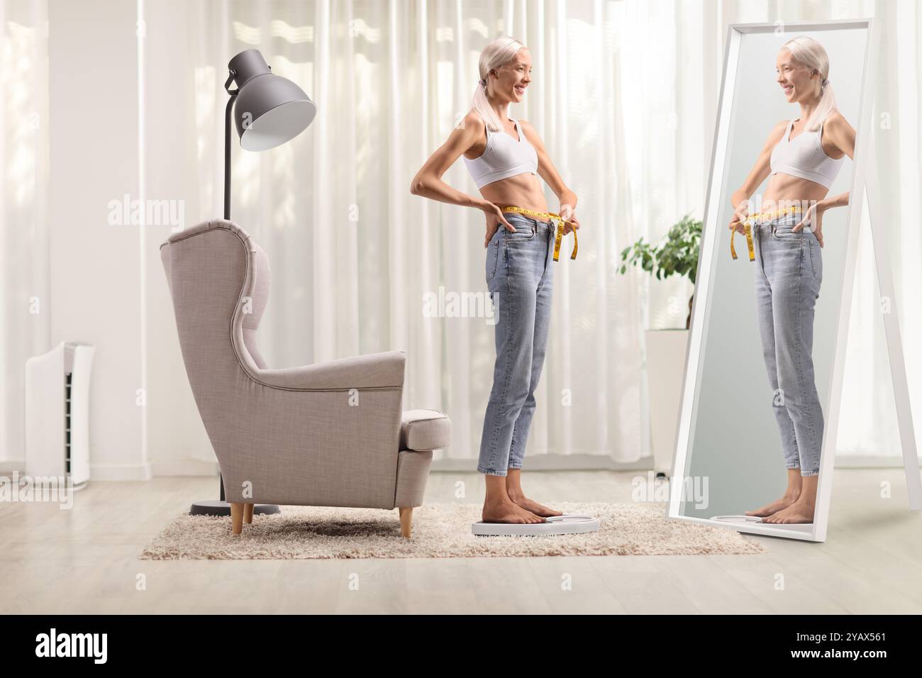 Tall slim woman in jeans and crop top measuring waste in front of ...