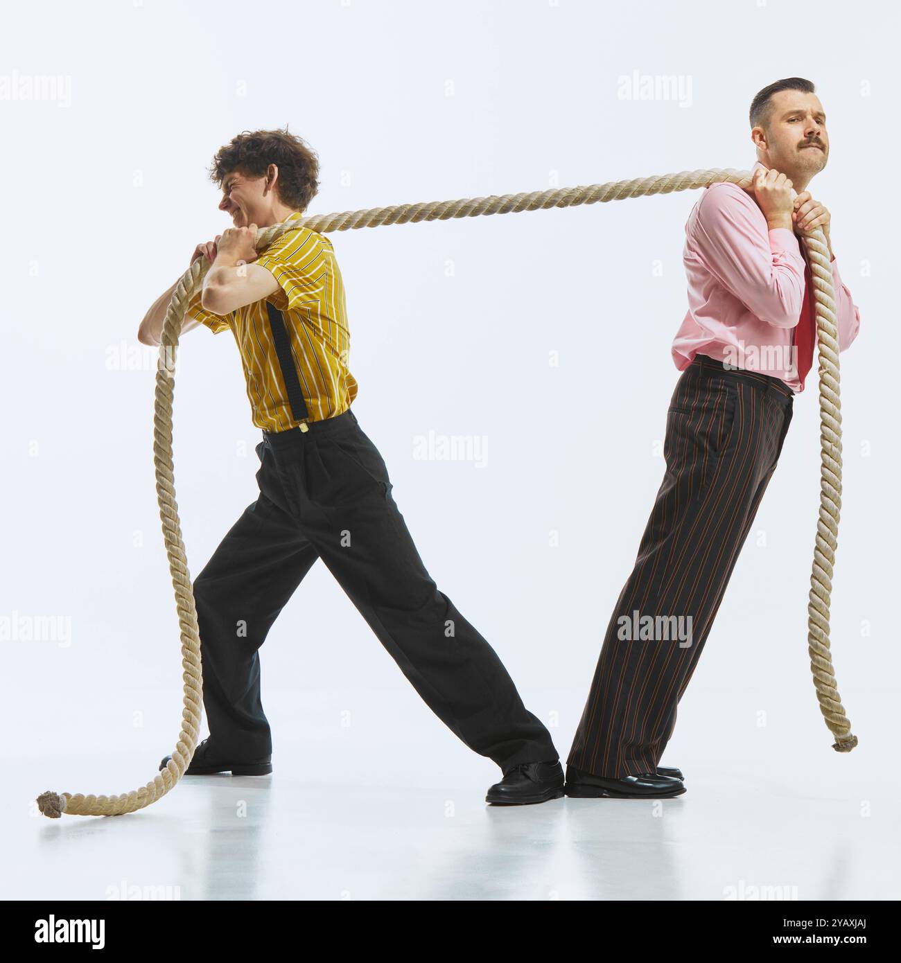 Two men engaged in tug of war, one pulling rope with all his strength ...