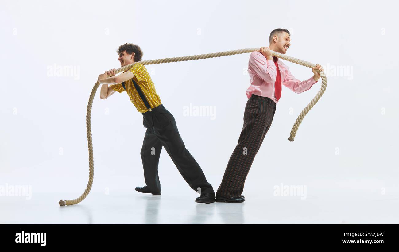 Two men engaged in tug of war, one pulling rope with all his strength ...