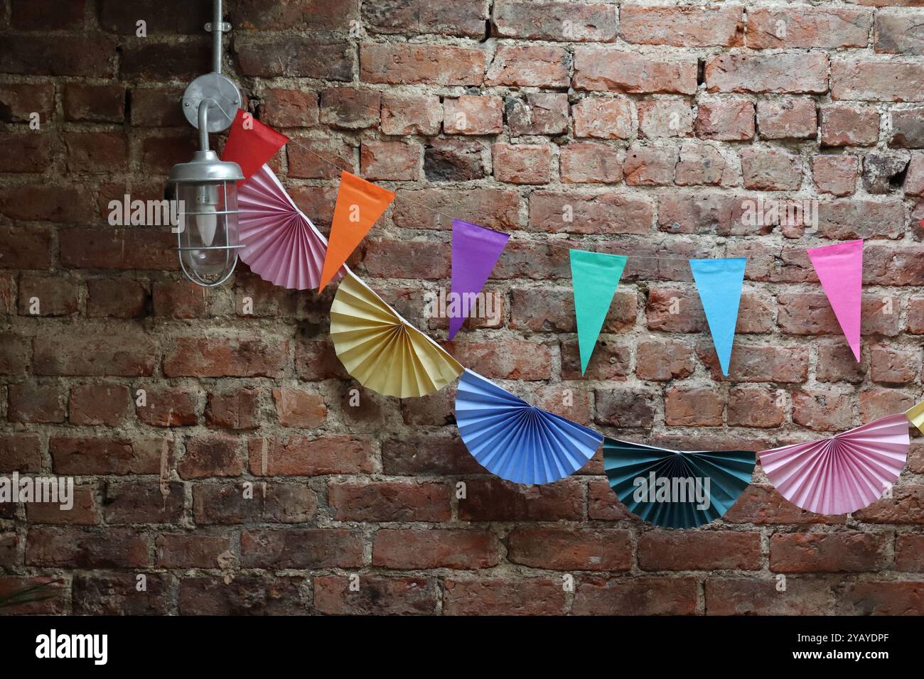 Colorful Paper Garland on Exposed Brick Wall with Hanging Light Stock ...