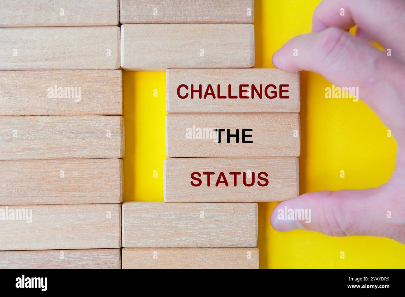 Hand pulling out wooden blocks with Challenge the Status text on yellow ...