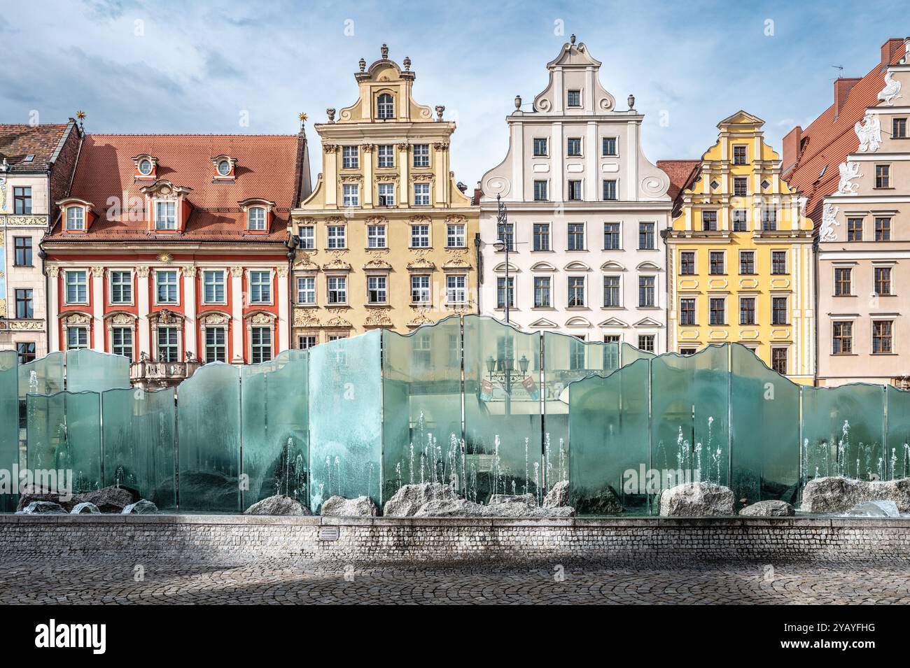 Colorful historic buildings tower over a unique glass fountain in a ...