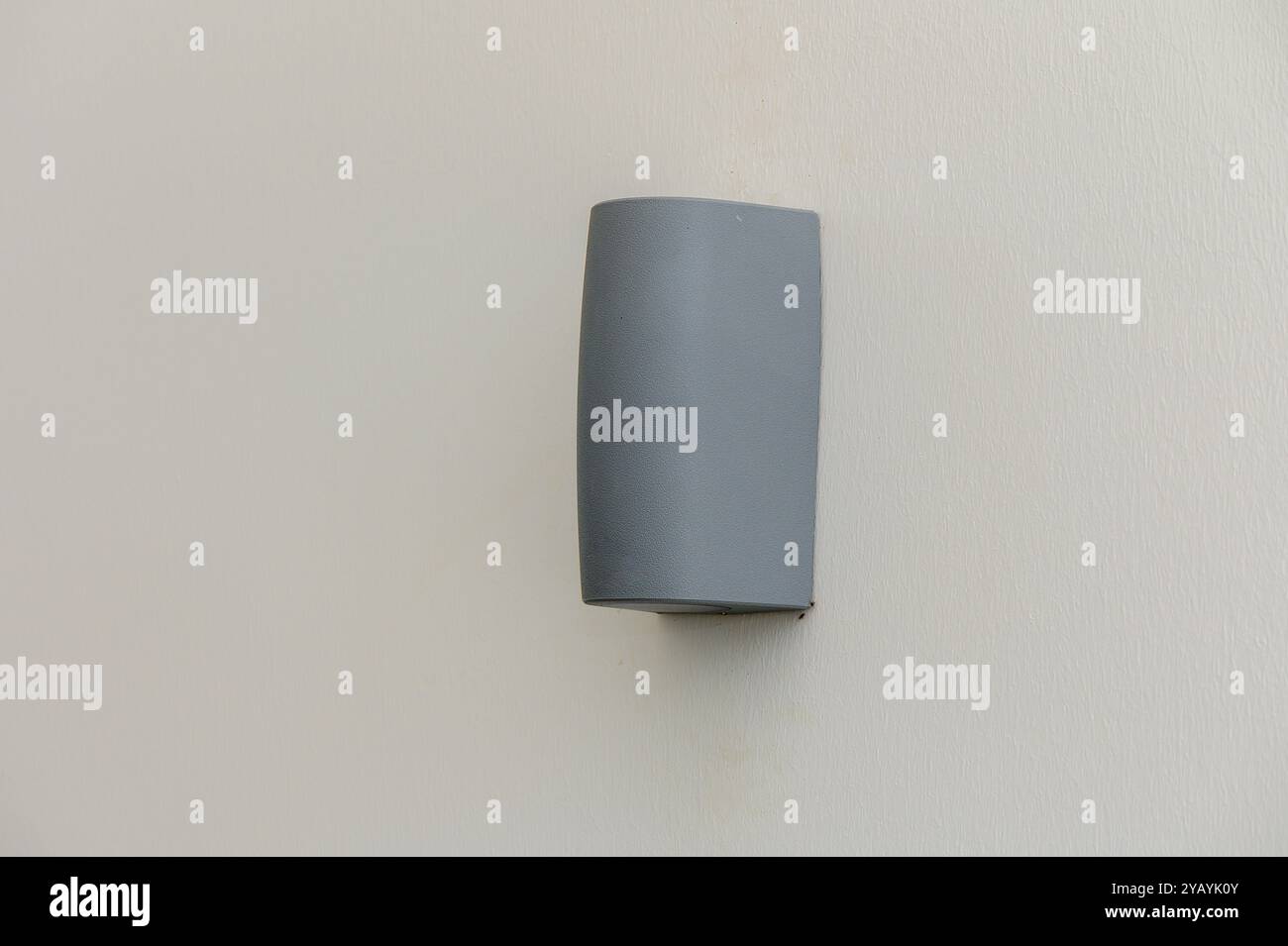 A contemporary gray wall-mounted light fixture stands against a pale ...