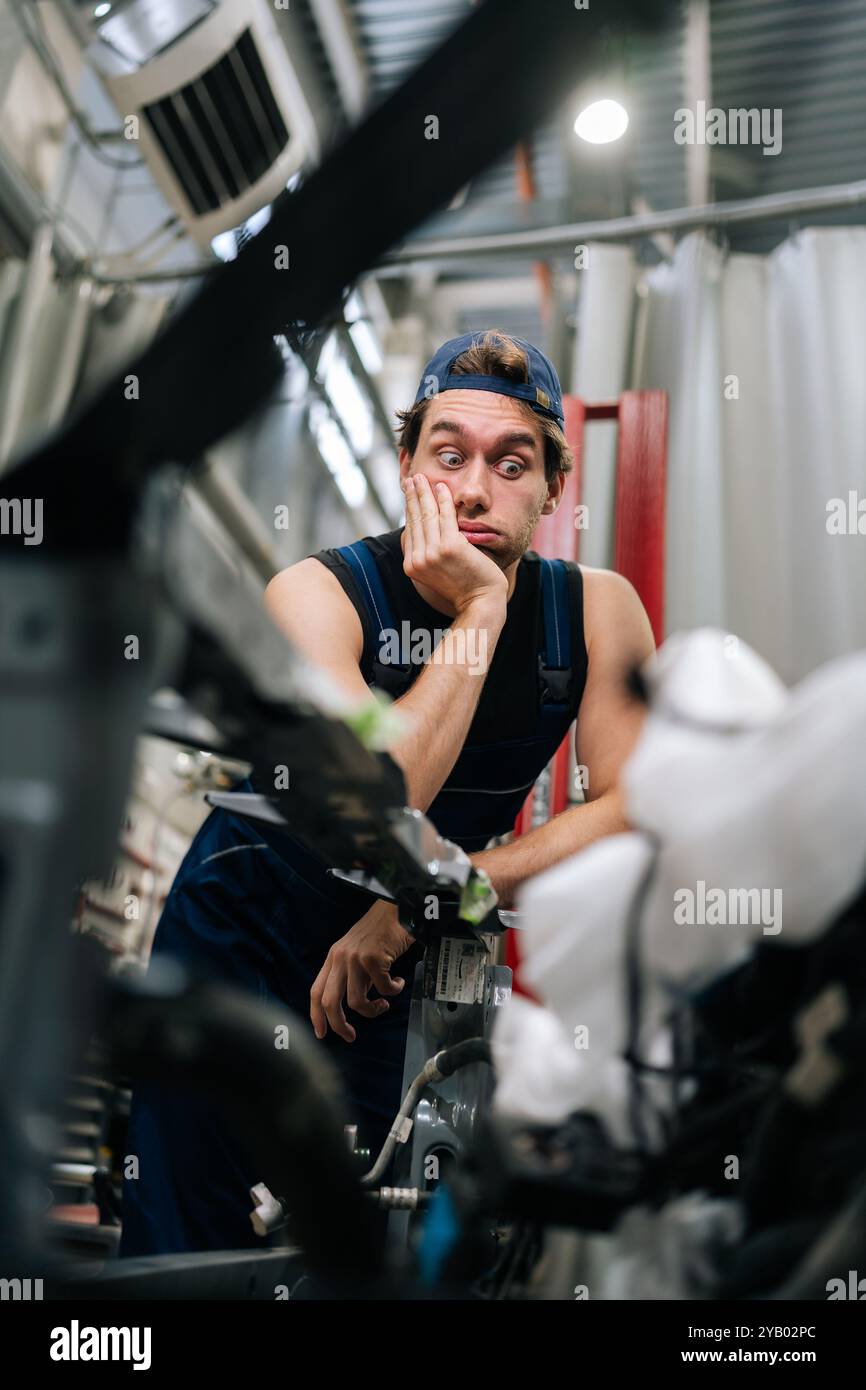 Vertical portrait of pensive young mechanic with confused expression ...