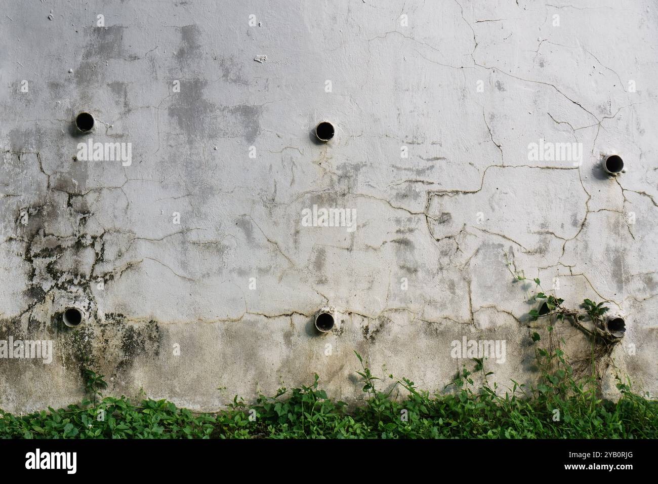 A weathered concrete wall with visible cracks and four weep holes ...