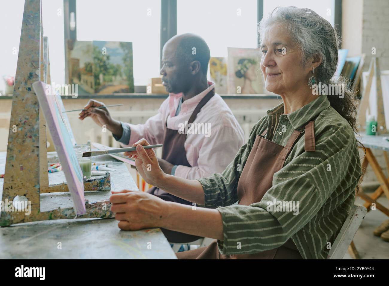 Retired biracial couple painting on canvases together during art ...