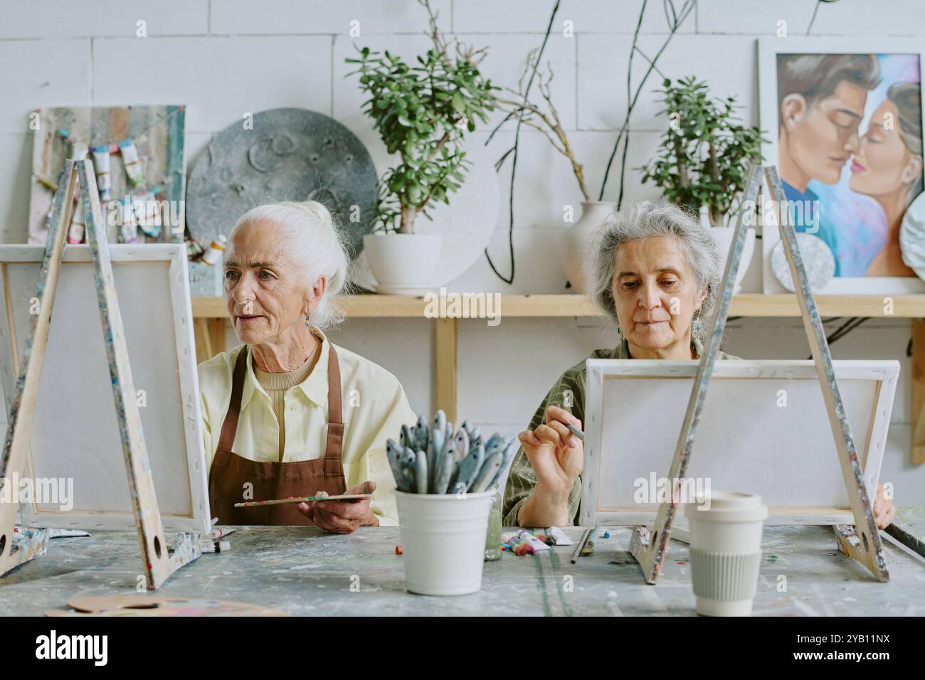 Two senior best friends painting on canvas together during art therapy ...