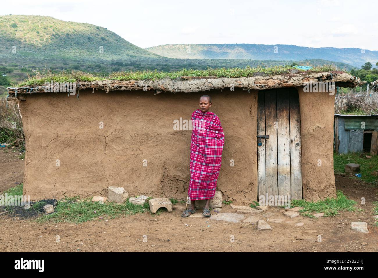Young Masai boy standing outside a traditional Masai dwelling house ...