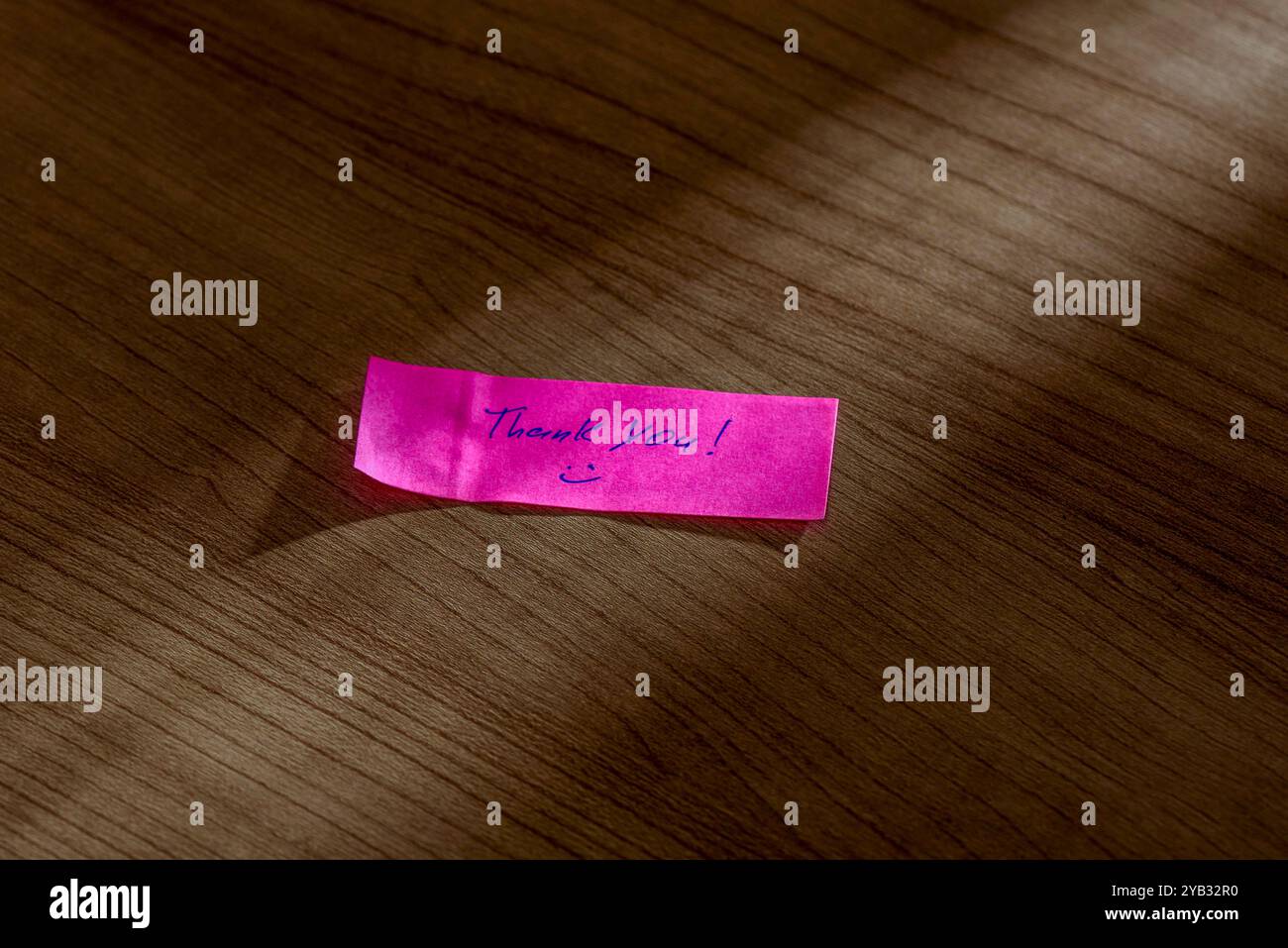 A pink sticky note with a handwritten message on a wooden background ...