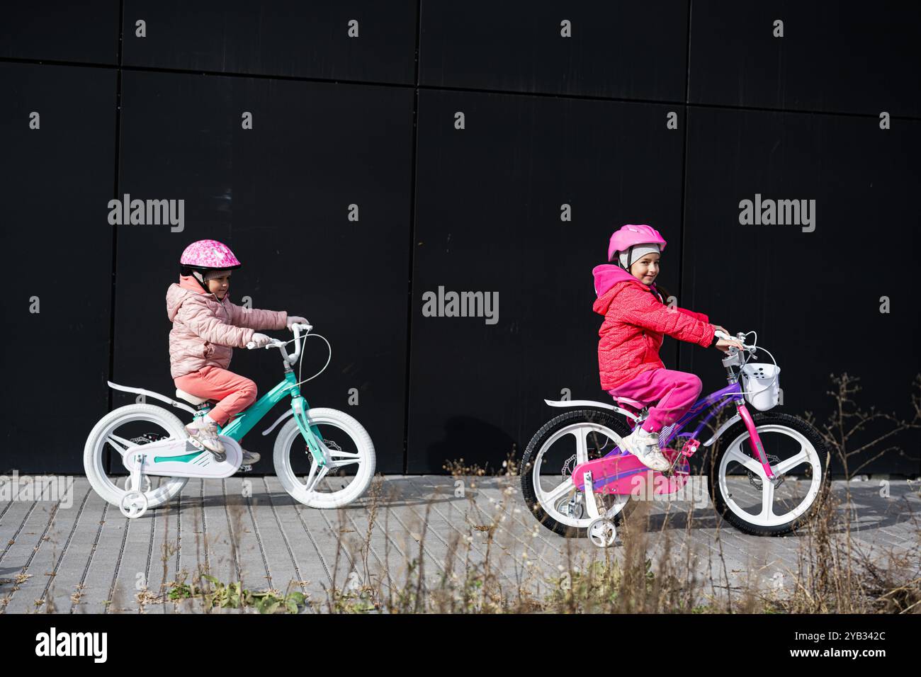 Two young girls in colorful jackets and helmets enjoy a sunny outdoor ...