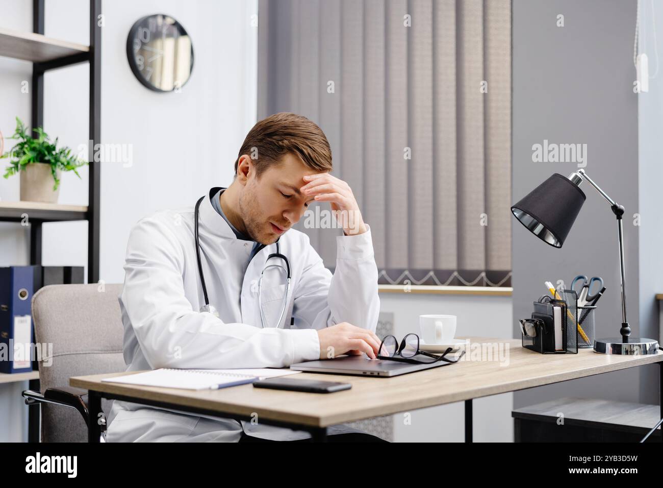 Handsome doctor man wearing medical uniform sitting on his workplace ...