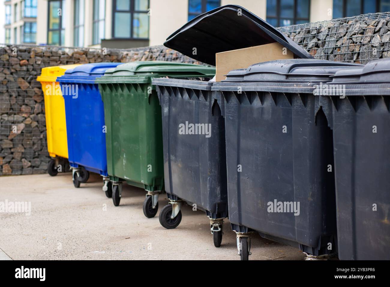 A neat row of colorful garbage cans is lined up in front of a tall ...