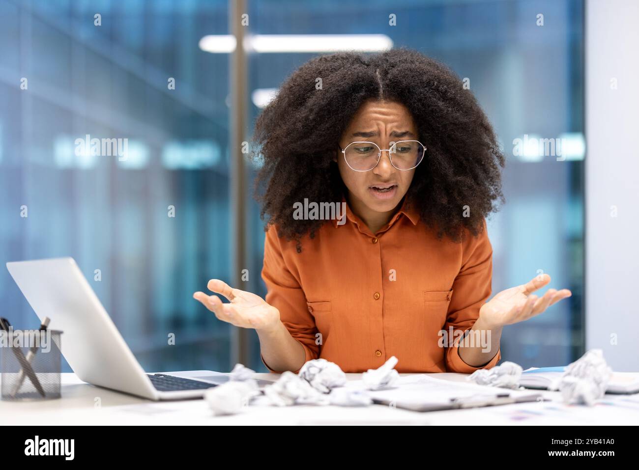 Frustrated woman in office surrounded by crumpled papers, laptop open ...