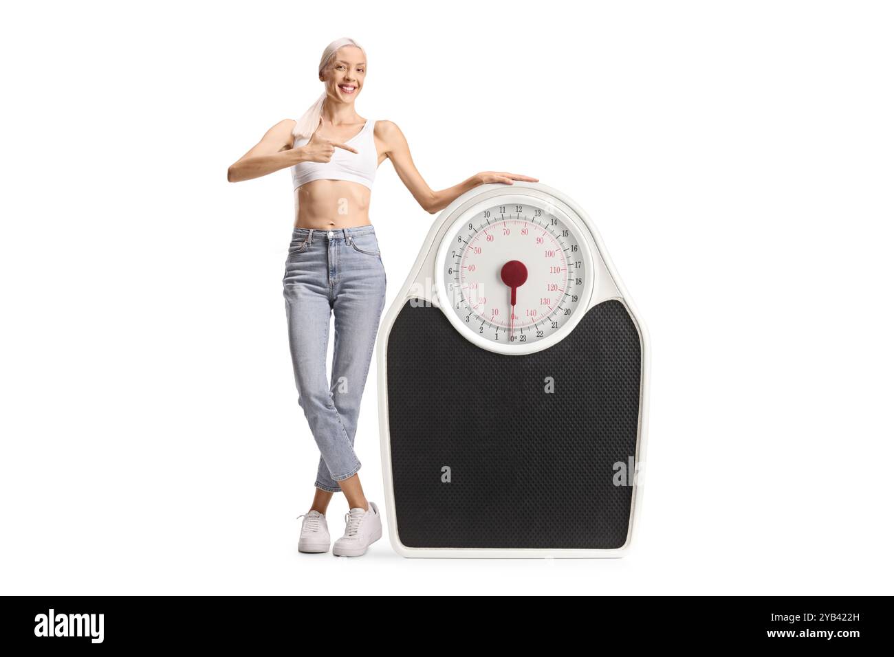 Happy woman in jeans and crop top standing pointing at a big weight ...