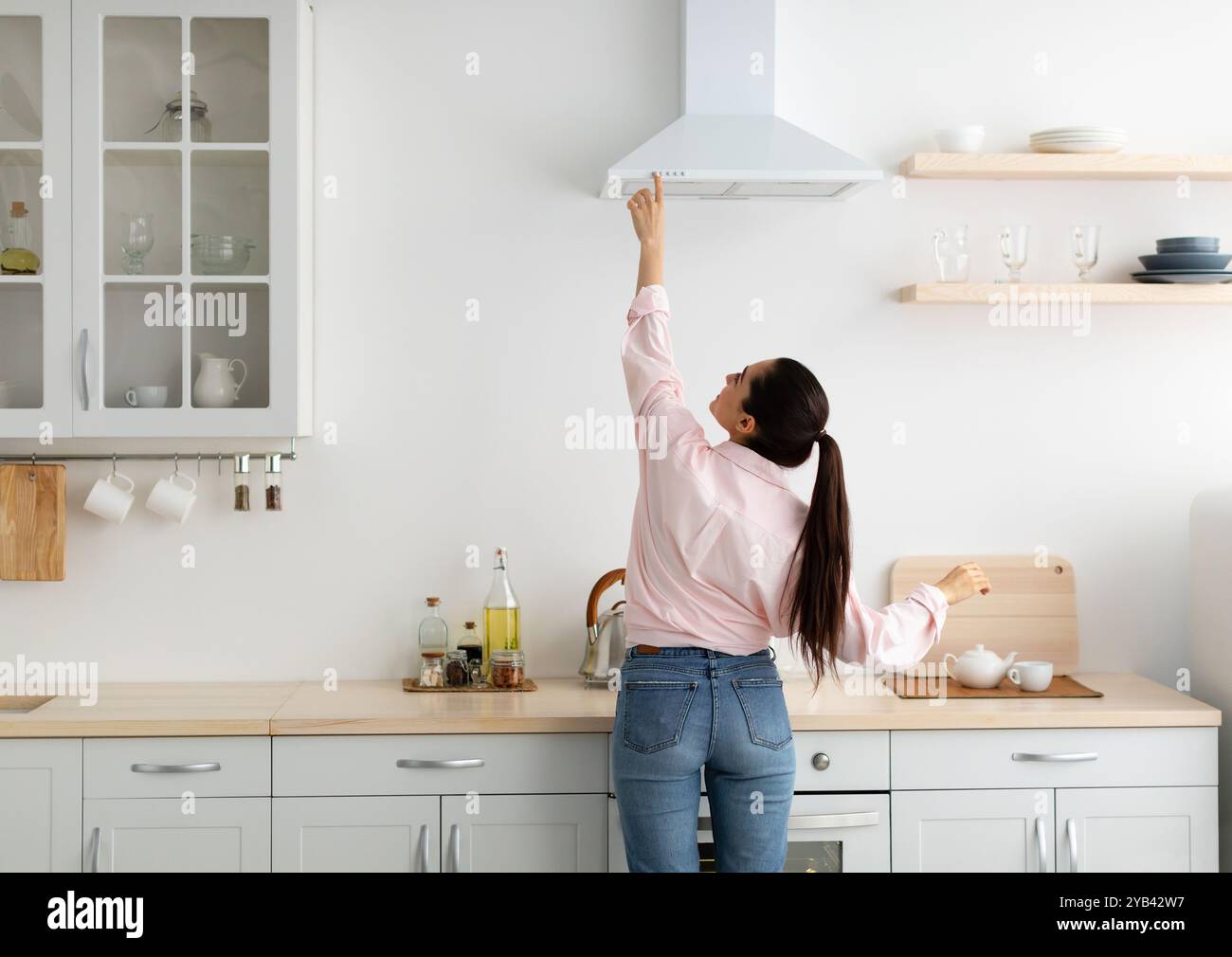 Back view woman select mode on cooking hood in kitchen Stock Photo - Alamy