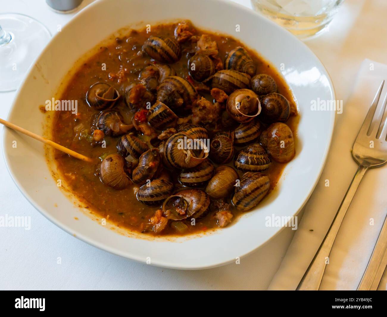 Stewed snails in red sauce served on a white ceramic plate close to the ...