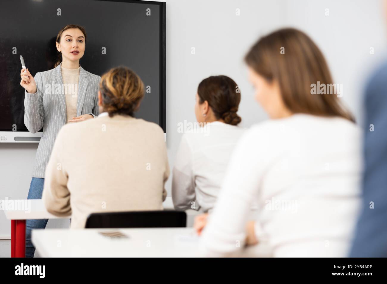 Young female professor explaining subject to classroom full of students ...