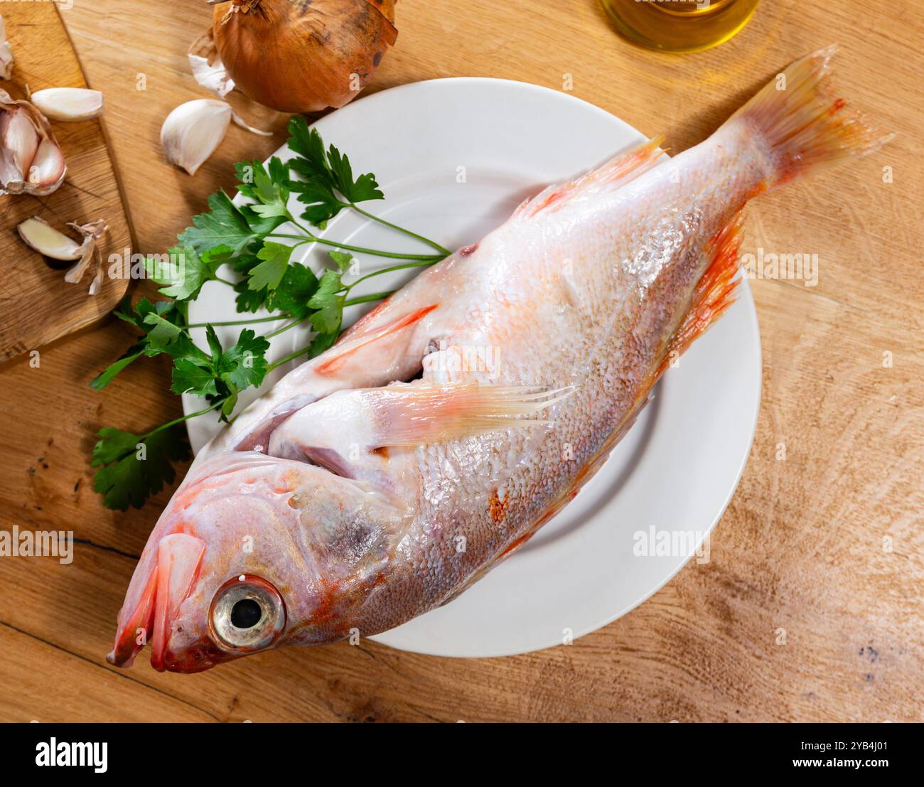 Raw whole red palometa fish with garlic and parsley on desk Stock Photo ...
