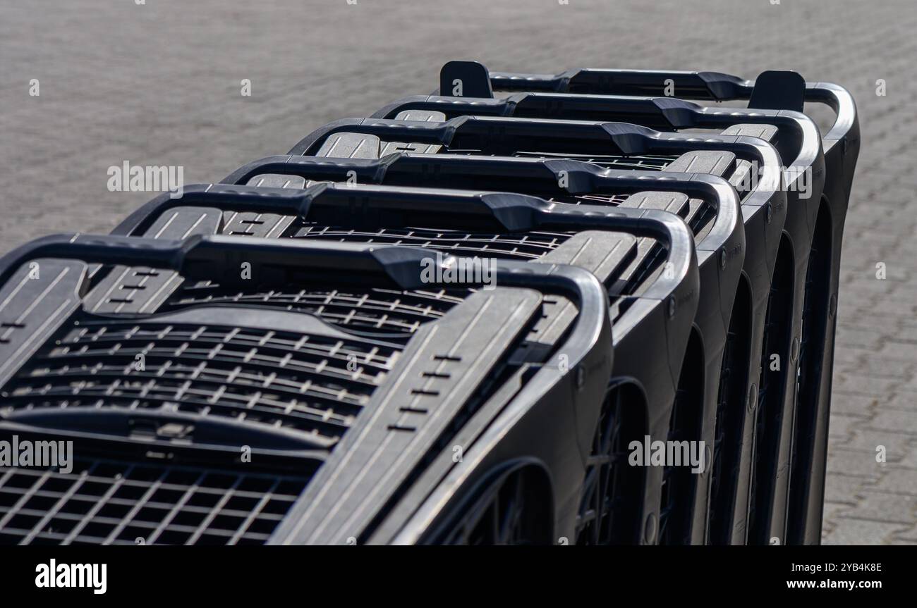 Several black recycling bins are neatly arranged in a row on a paved ...
