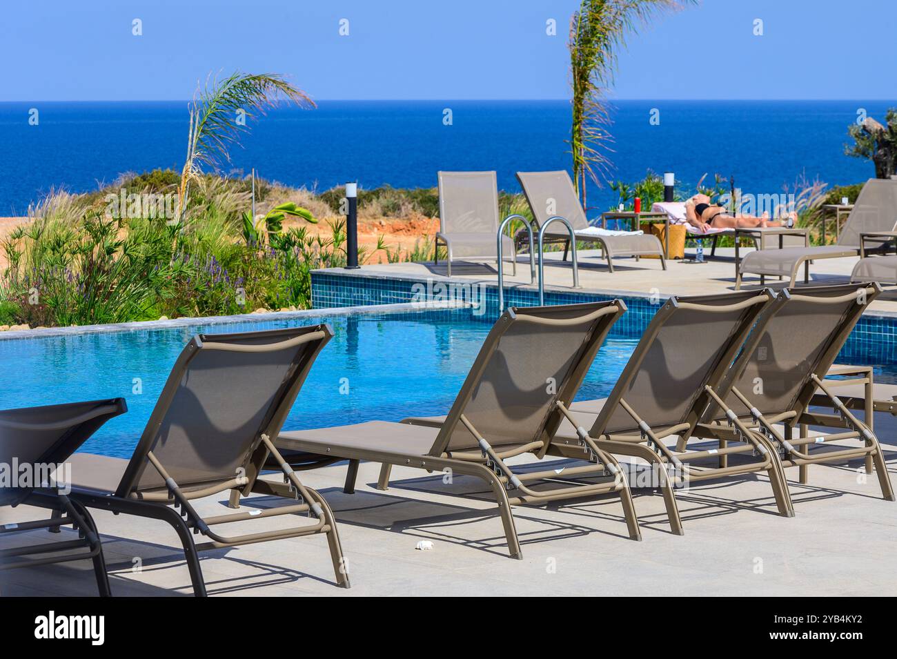 A tranquil pool area lined with lounge chairs overlooks the ocean ...